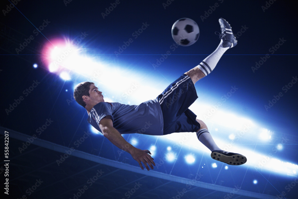Soccer player in mid air kicking the soccer ball, stadium lights at ...