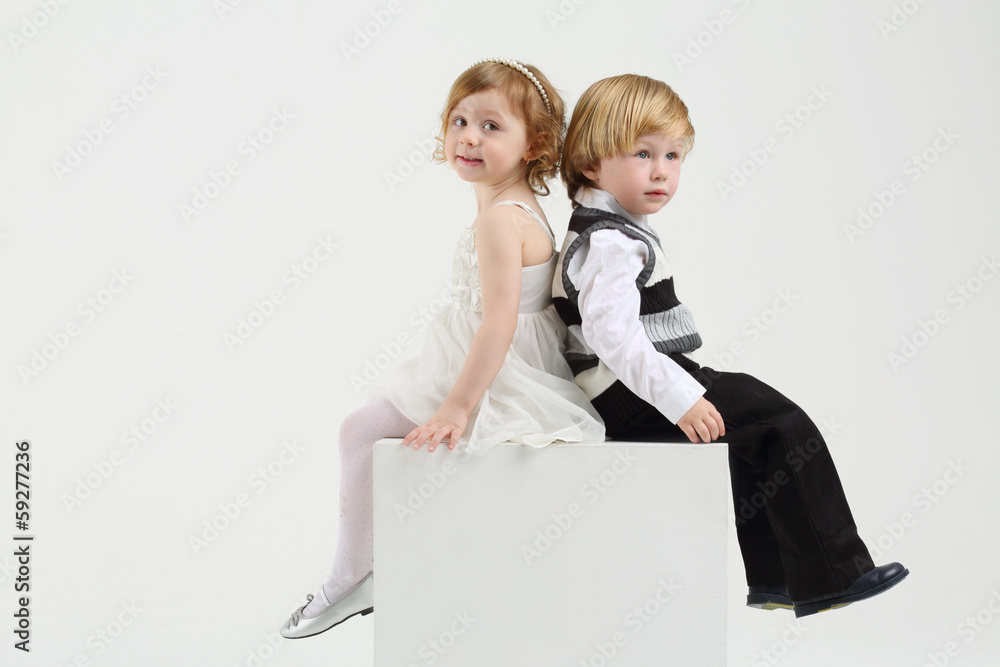Little happy girl and boy sit back to back on white big cube Stock ...