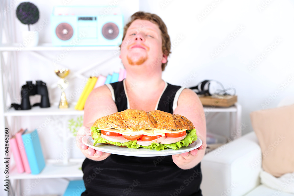 Fat man eating tasty sandwich on home interior background Stock Photo ...