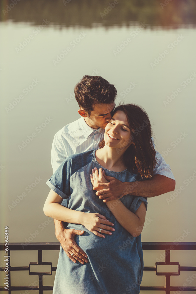 Happy and young pregnant couple hugging in nature at the lake. V Stock ...