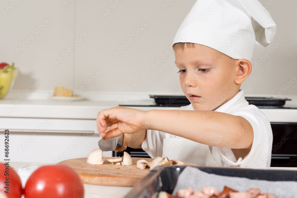 Cute little boy in a chefs toque slicing mushrooms Stock Photo | Adobe ...