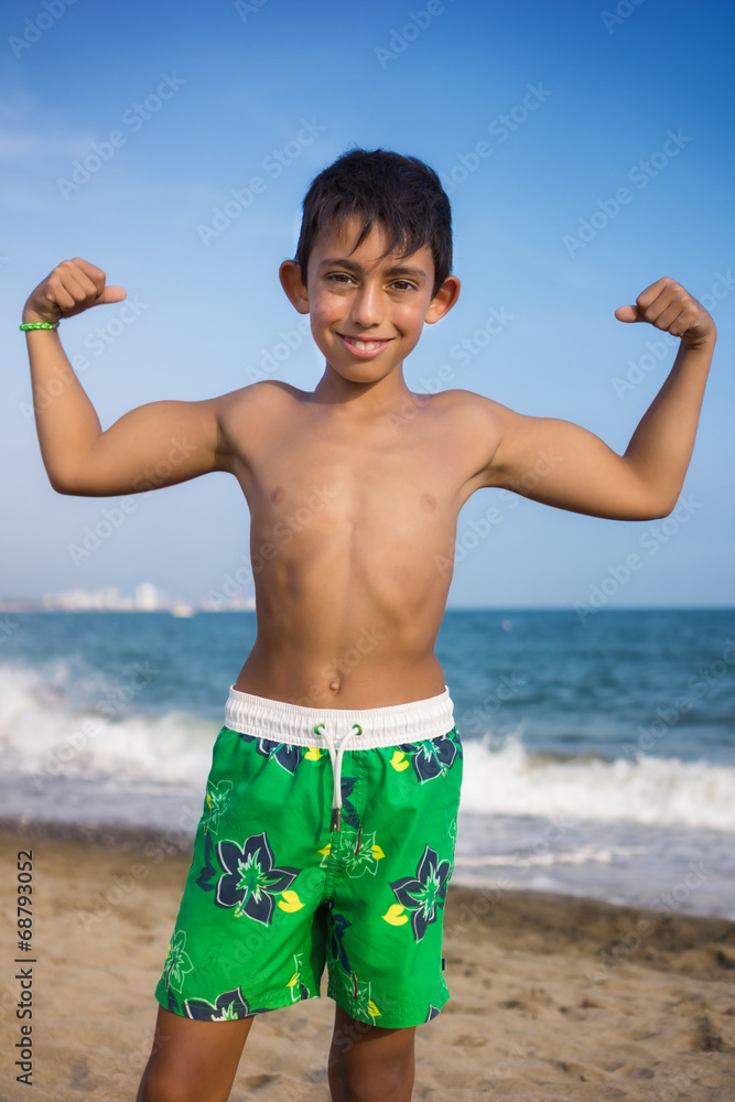 little boy showing his muscles on the beach Photos | Adobe Stock