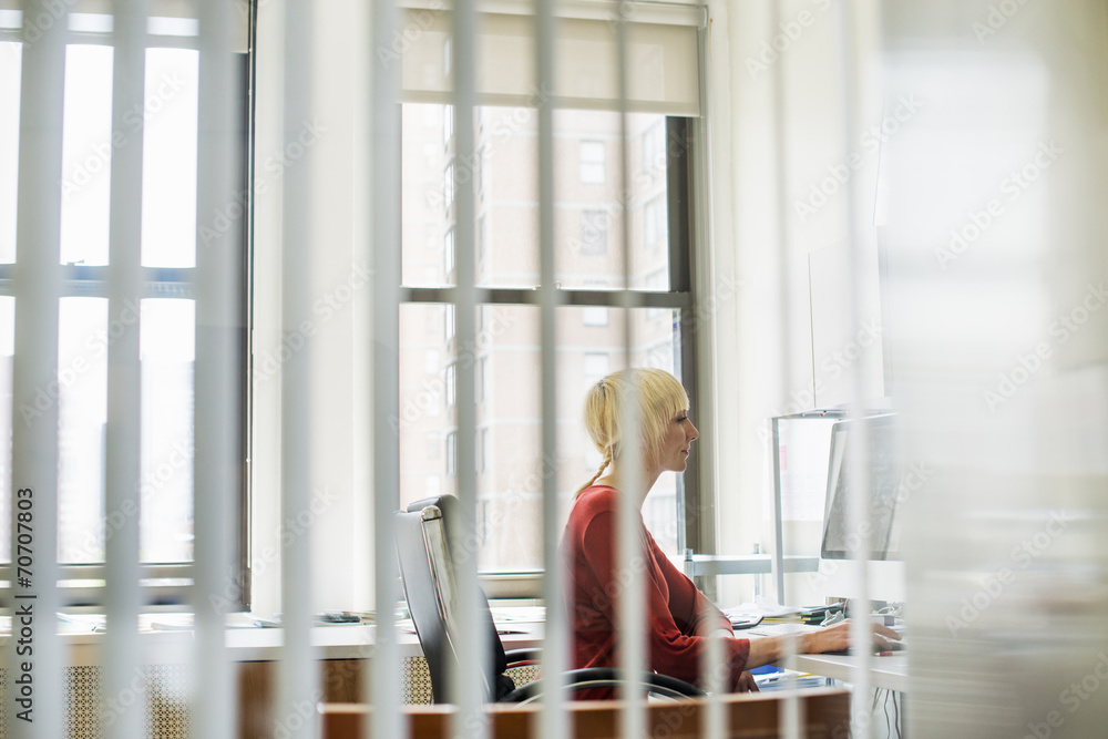 Office life. A woman sitting at a desk using a computer, looking ...