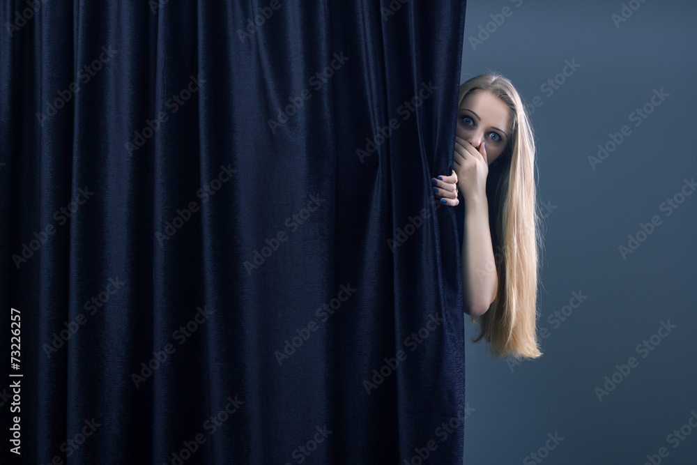 Frightened girl hiding behind a curtain. Stock Photo | Adobe Stock