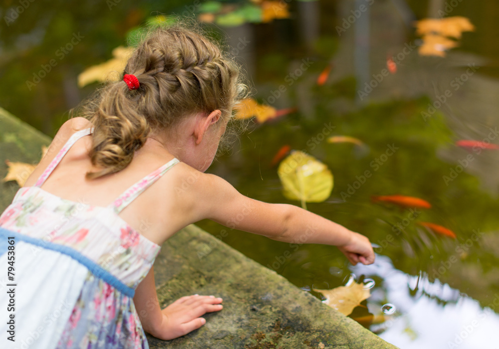 Little girl sitting by the pond with fish. Stock Photo | Adobe Stock