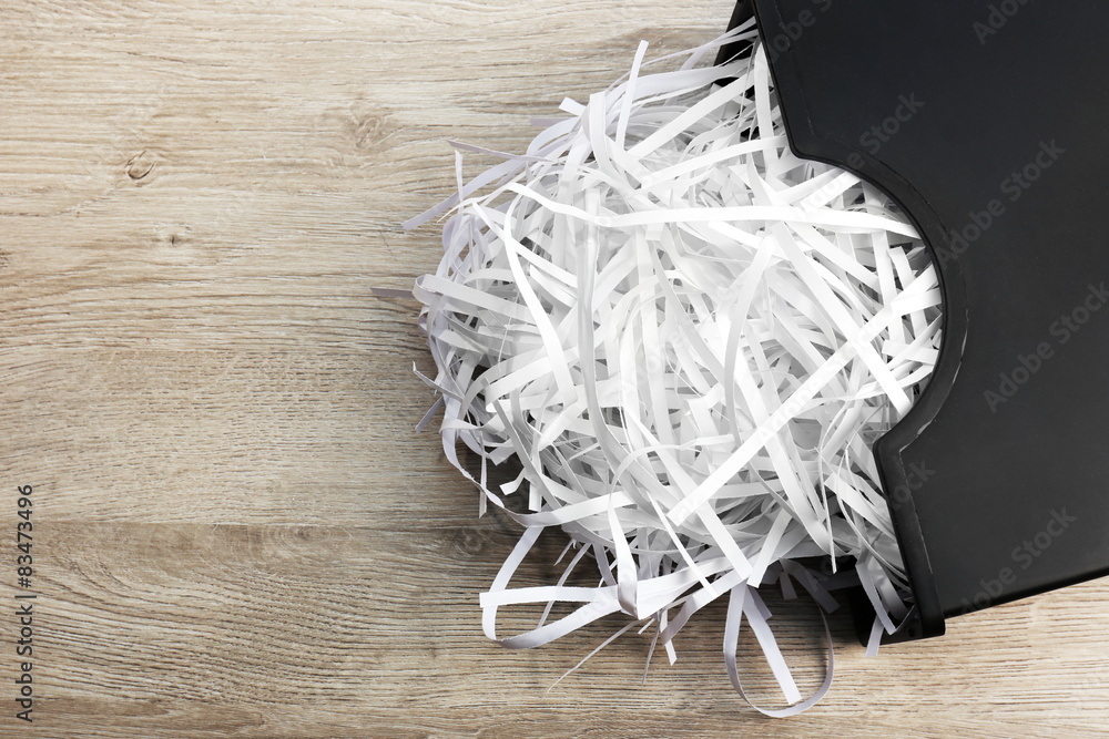 Strips of destroyed paper from shredder in trash can on wooden ...