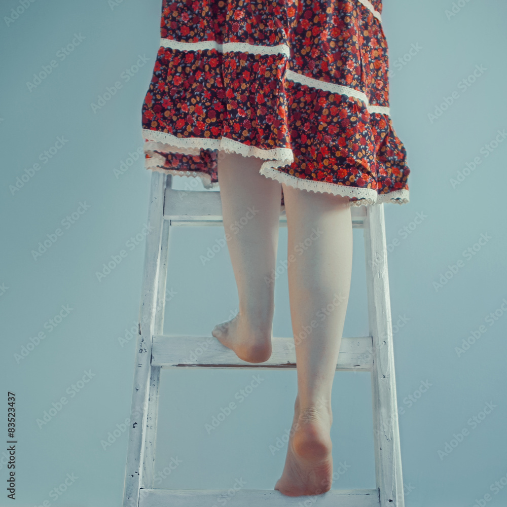 Rear view of a barefoot Woman in a dress climbing a step ladder Stock ...