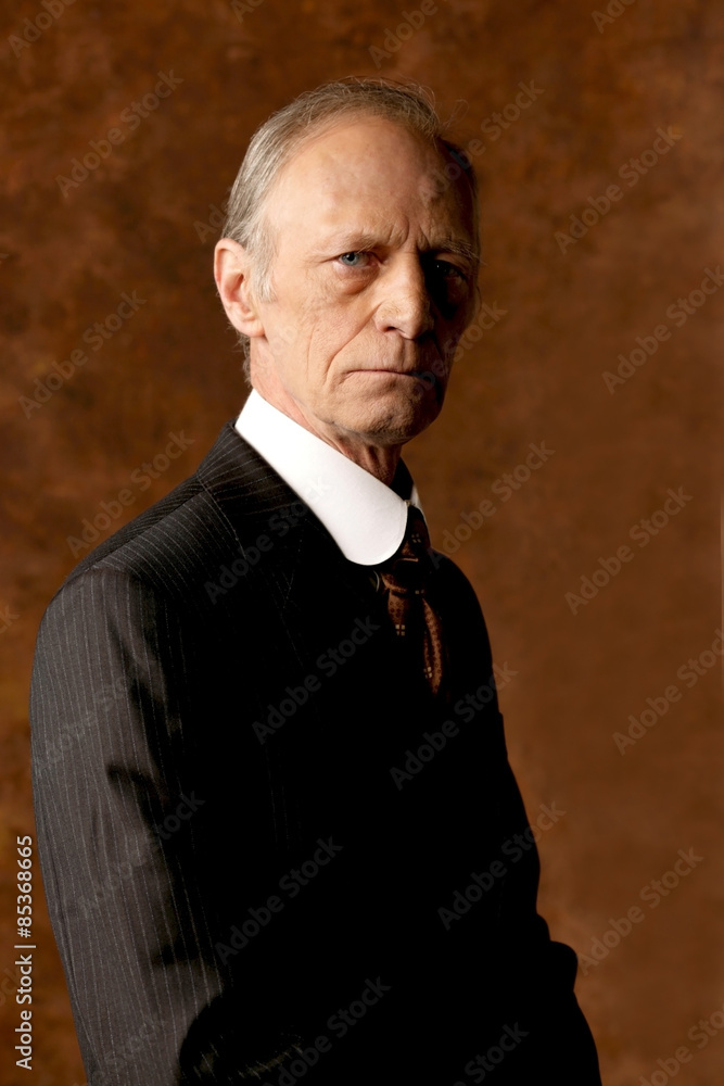 Studio portrait of a well dressed old man on a mottled brown canvas ...