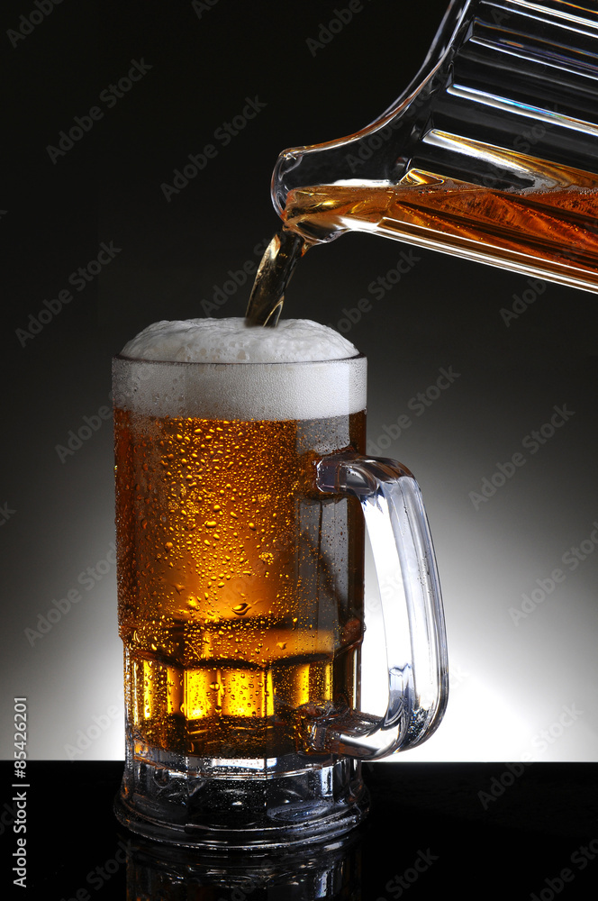 Closeup of a beer mug being filled from a pitcher pouring cold ale into ...