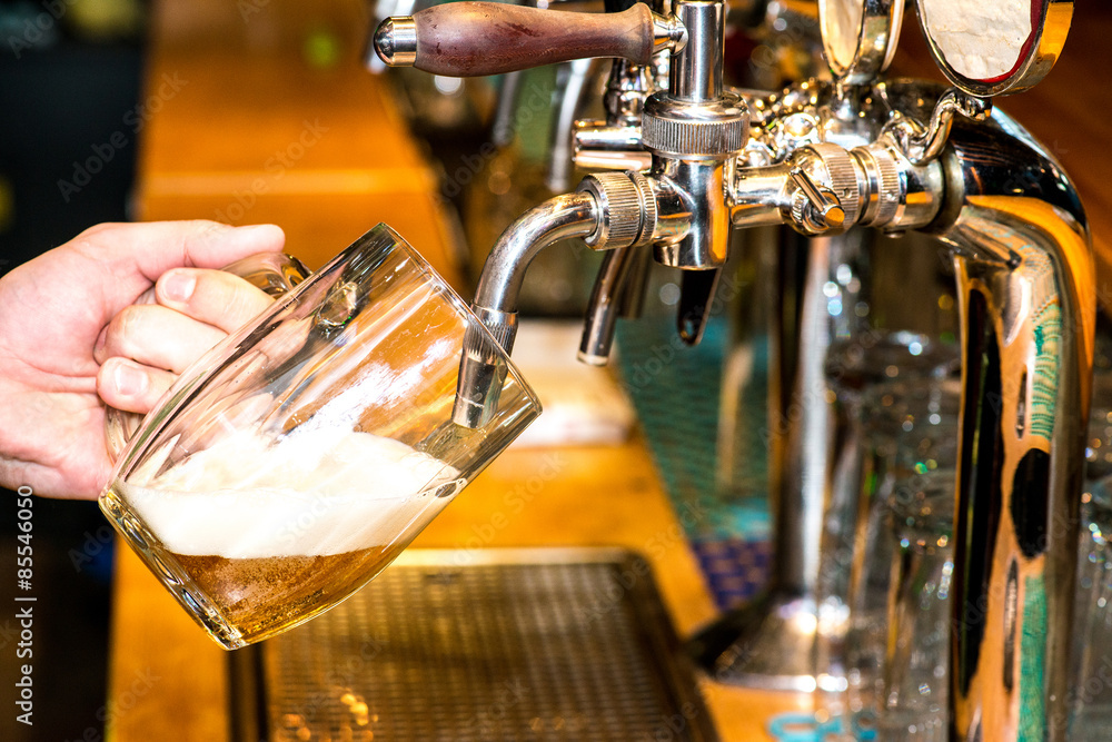 Poster Close-up of bartender hand at beer tap pouring a draught lager ...