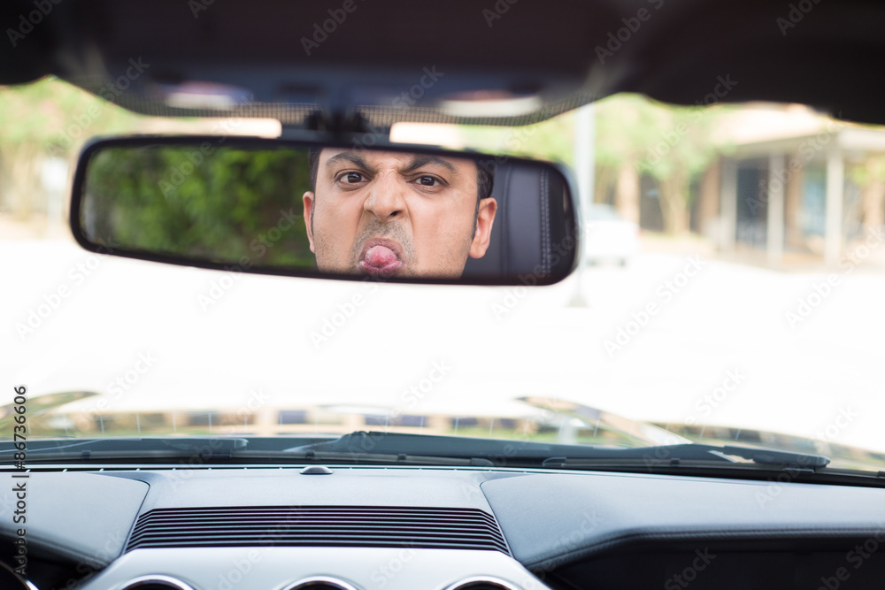 Closeup portrait, angry young driver making stupid faces in rearview ...