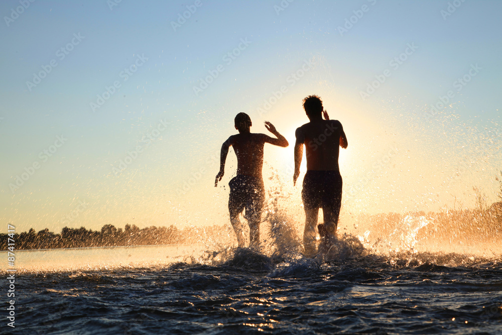 Glückliche junge Menschen laufen und springen am See beim ...