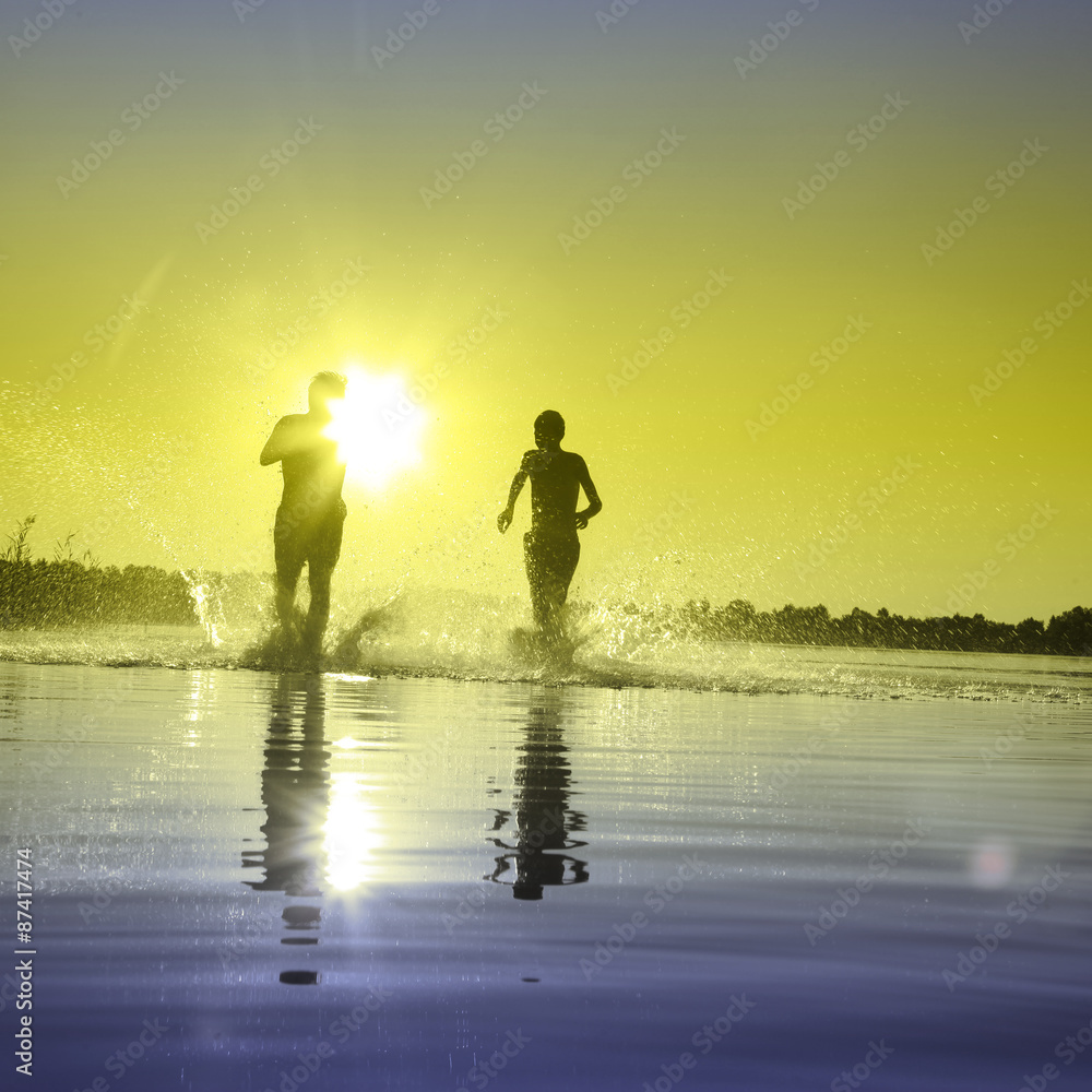 Glückliche junge Menschen laufen und springen am See beim ...
