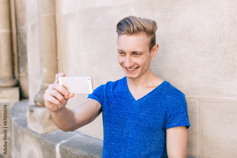 Young handsome man with short hair taking a selfie in an urban context ...