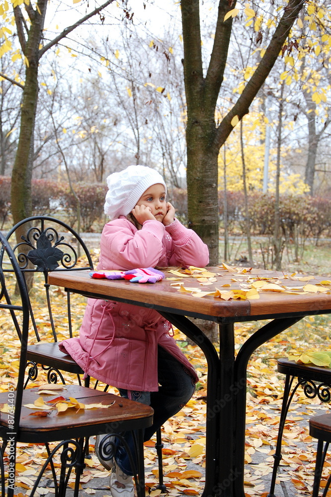 sad girl in the autumn. little girl sitting alone at a table cafe ...