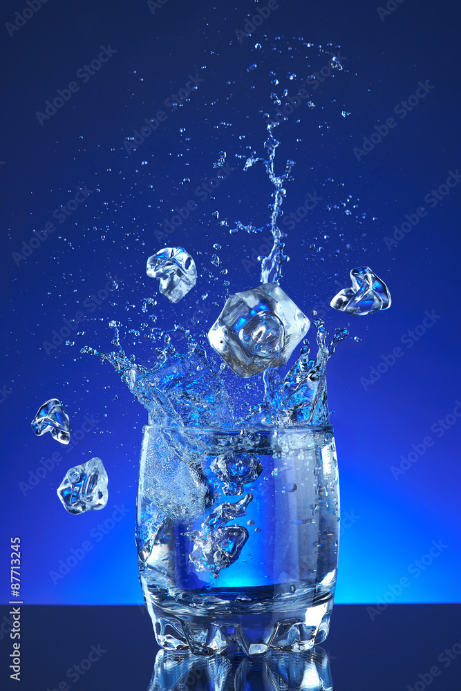 Ice and Water poured into a glass, splash, blue background, refreshing ...