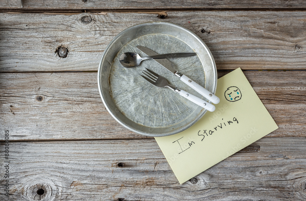 horizontal conceptual image of an empty tin plate with cutlery and a ...