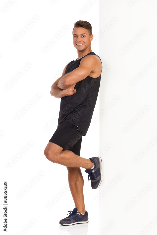 Man Rests Against The Wall. Smiling young man in sport black shirt and ...