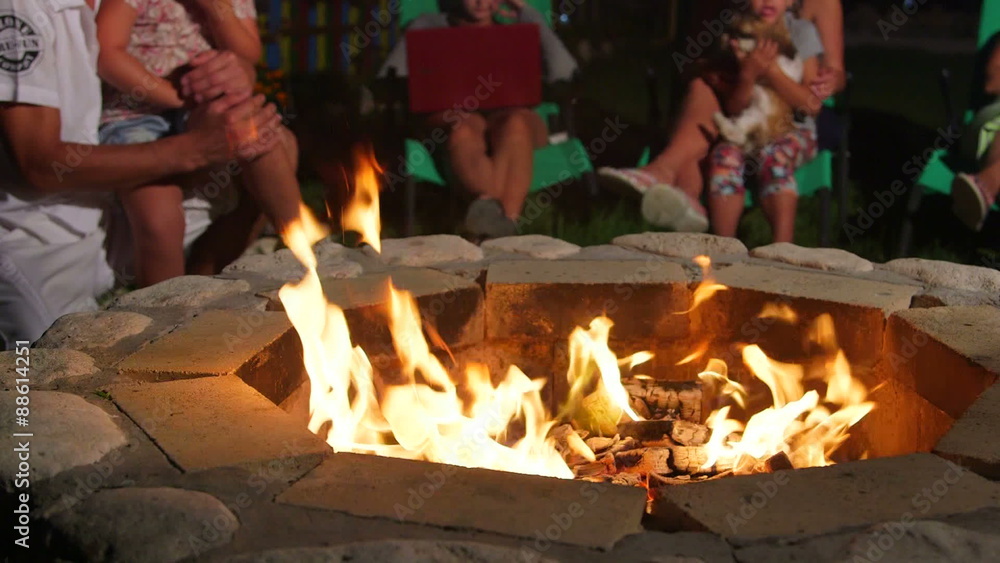 Group of people sitting on patio loungers around stone fire pit in back ...