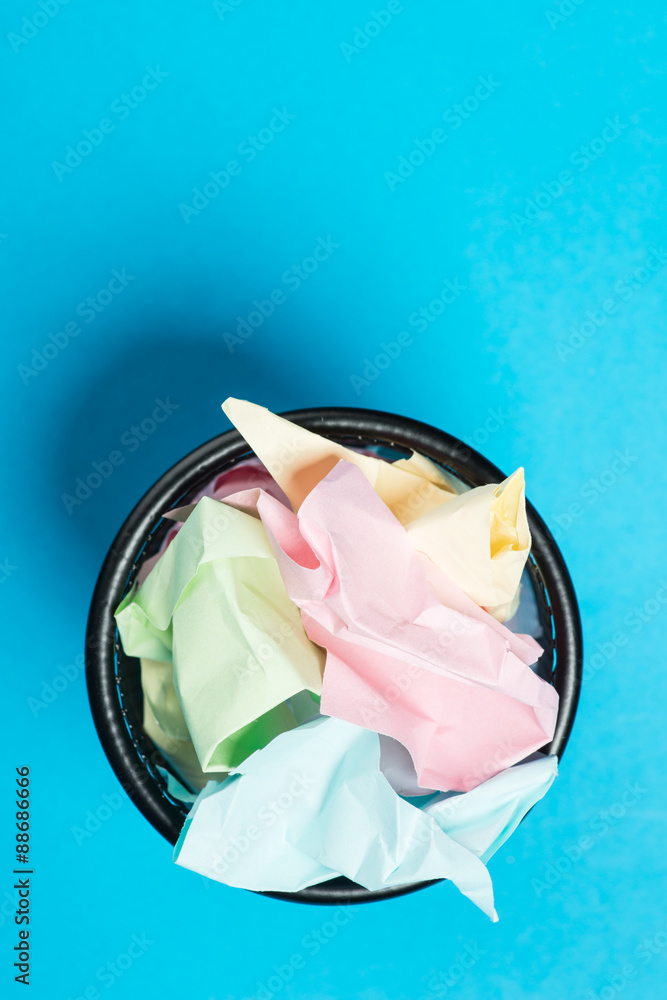 Colorful crumpled paper in a black garbage bin over the blue background ...