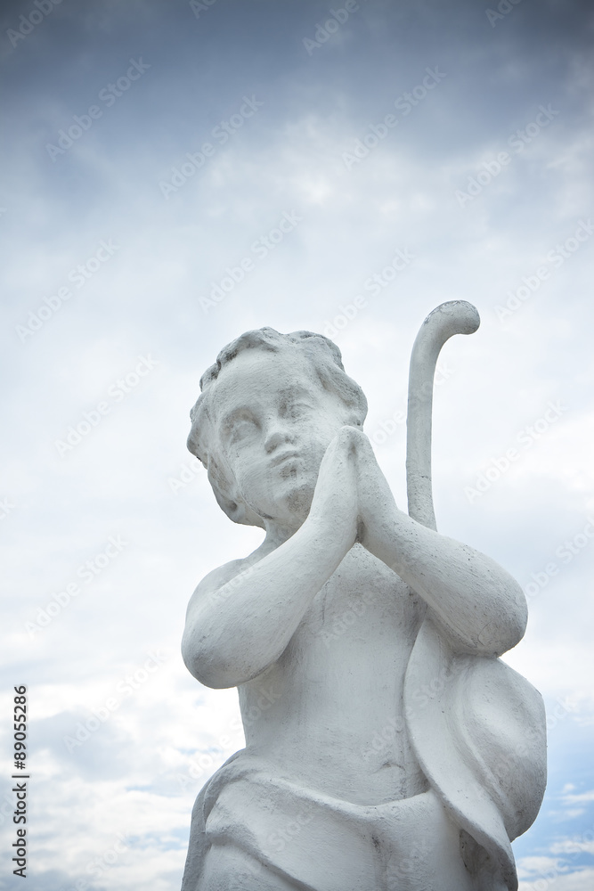 Statue of a cherub praying against blue sky. More than 100 years old ...