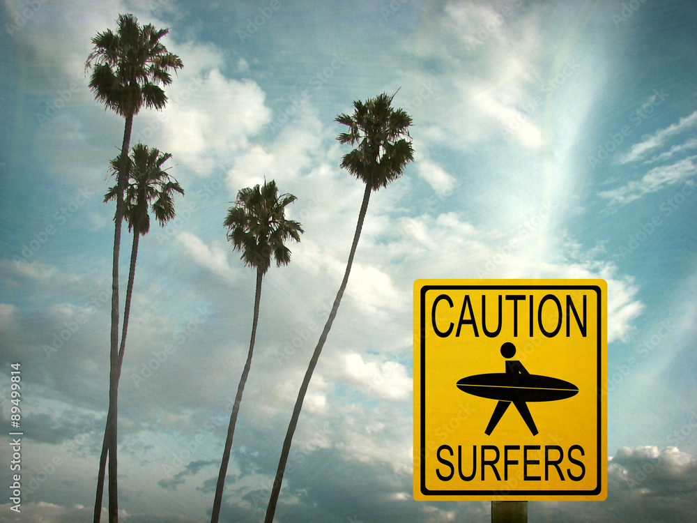 aged and worn vintage photo of caution surfer sign at beach with palm ...