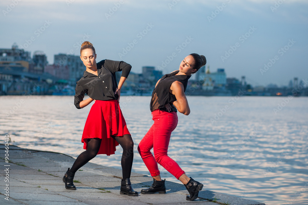 Two young beautiful twin sisters are dancing waacking dance in the city ...