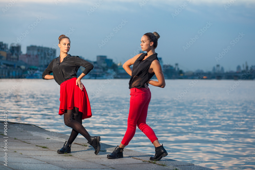 Two young beautiful twin sisters are dancing waacking dance in the city ...