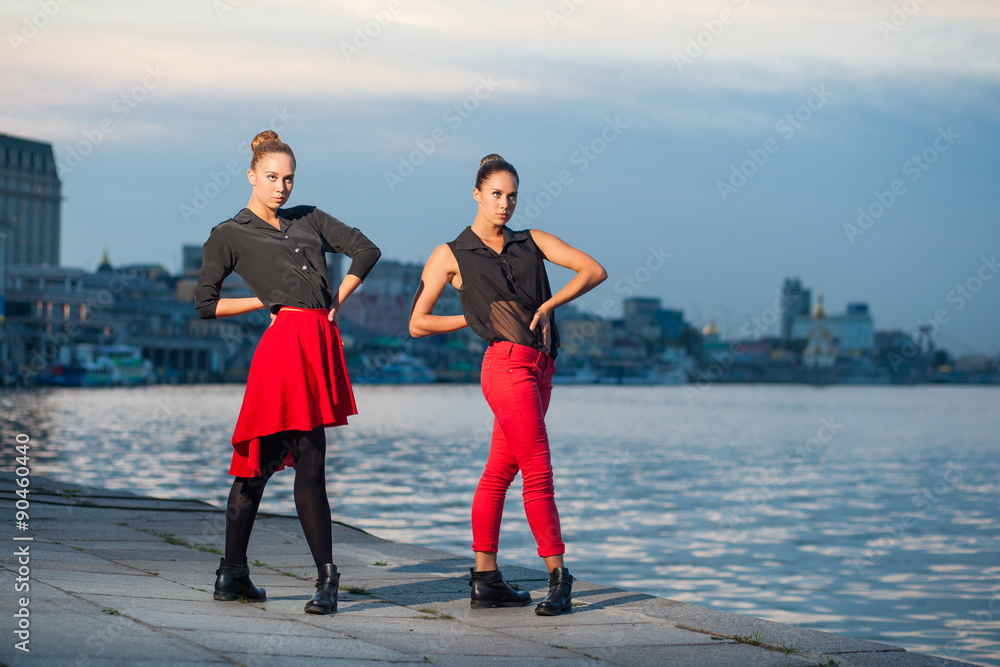 Two young beautiful twin sisters are dancing waacking dance in the city ...