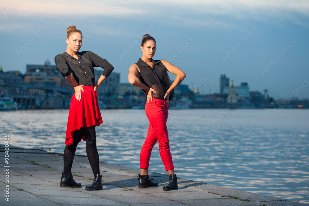 Two young beautiful twin sisters are dancing waacking dance in the city ...