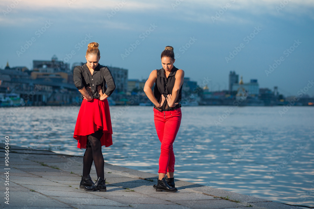 Two young beautiful twin sisters are dancing waacking dance in the city ...