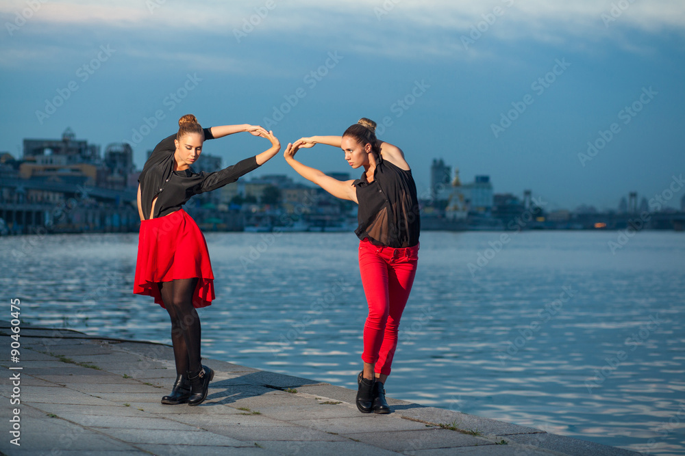 Two young beautiful twin sisters are dancing waacking dance in the city ...