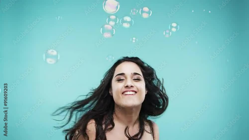 Crazy face busty Indian woman dancing in bubble shower slow motion photo booth blue background ...