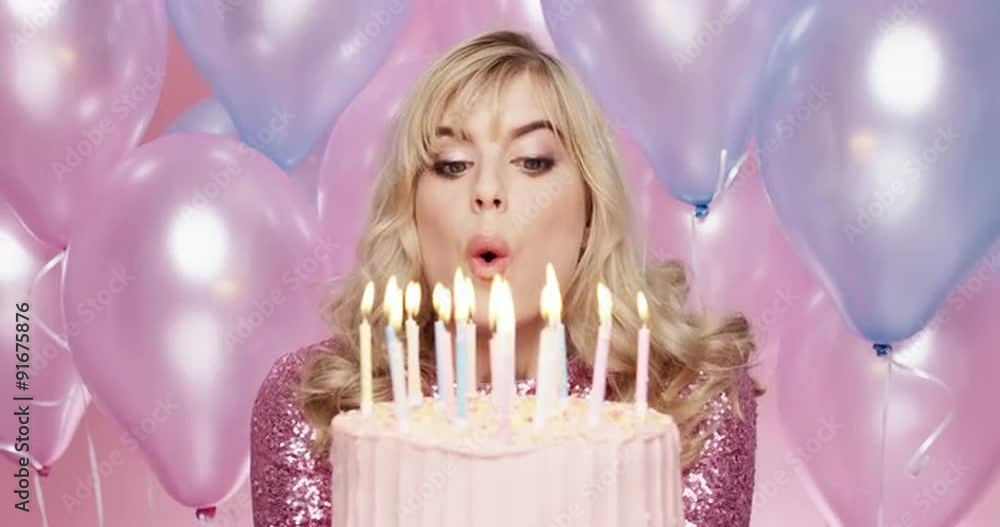 Beautiful young woman blowing out candles celebrating birthday pink and ...