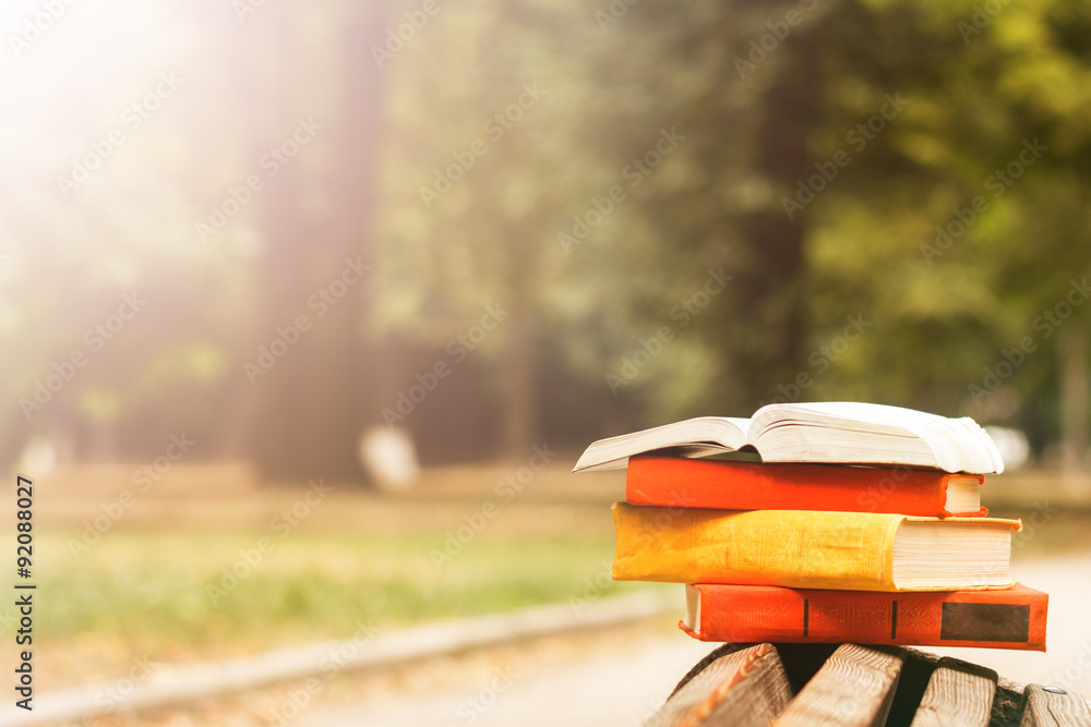 Stack of hardback book and Open book lying on a bench at sunset park on ...