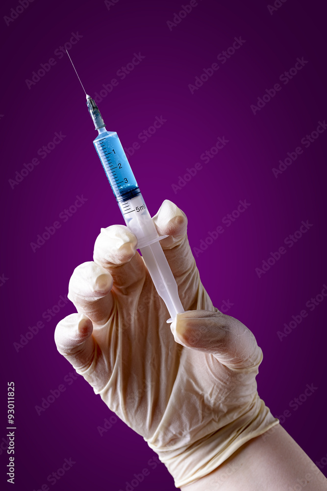 hand with surgical glove and syringe for injection on violet background ...