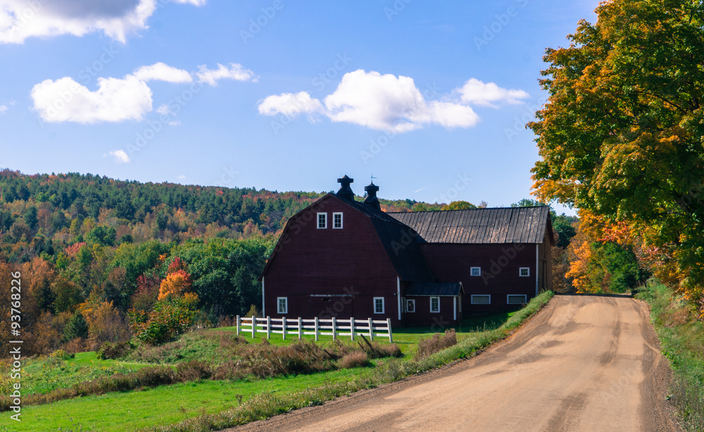 country road going through a farm with dark red barn and white fence ...