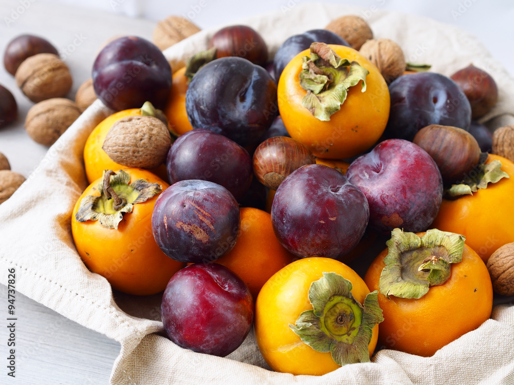 Persimmons with purple plums, chestnuts and walnuts. Fall still life ...