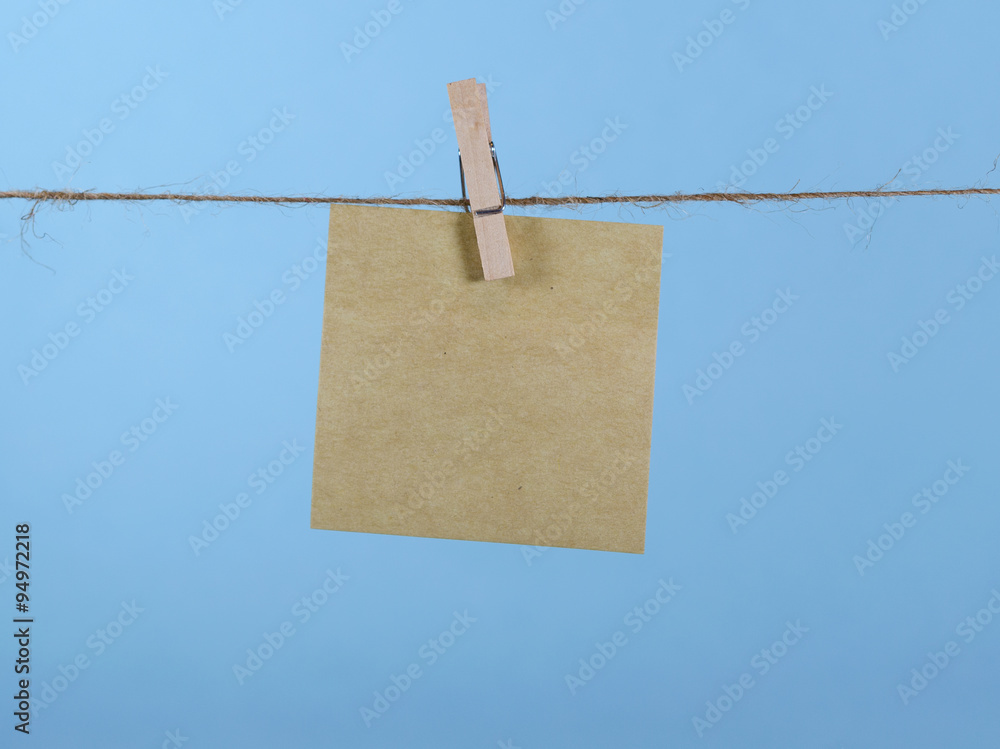 Empty old paper note hanging on a rope attached with pegs on a blue ...