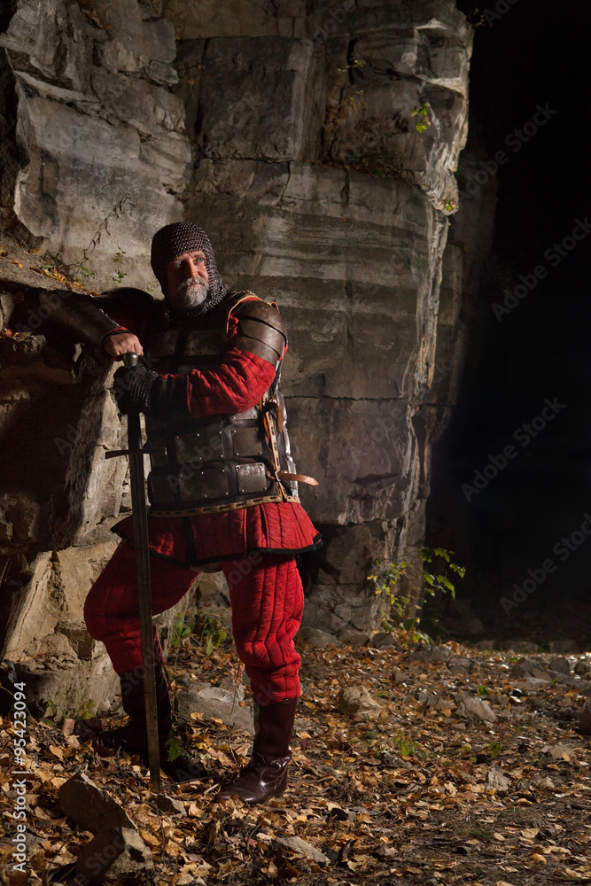 Old medieval King in armor with sword on the rocks background. Stock ...