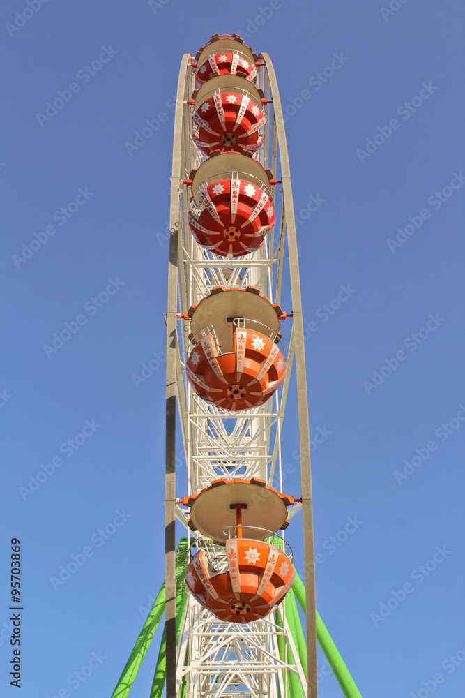 Side view of ferris wheel with colorful gondolas and blue sky ...