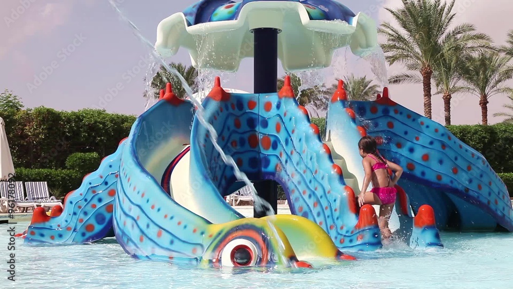 Little girl having fun riding a water slide in a swimming pool vídeo do ...