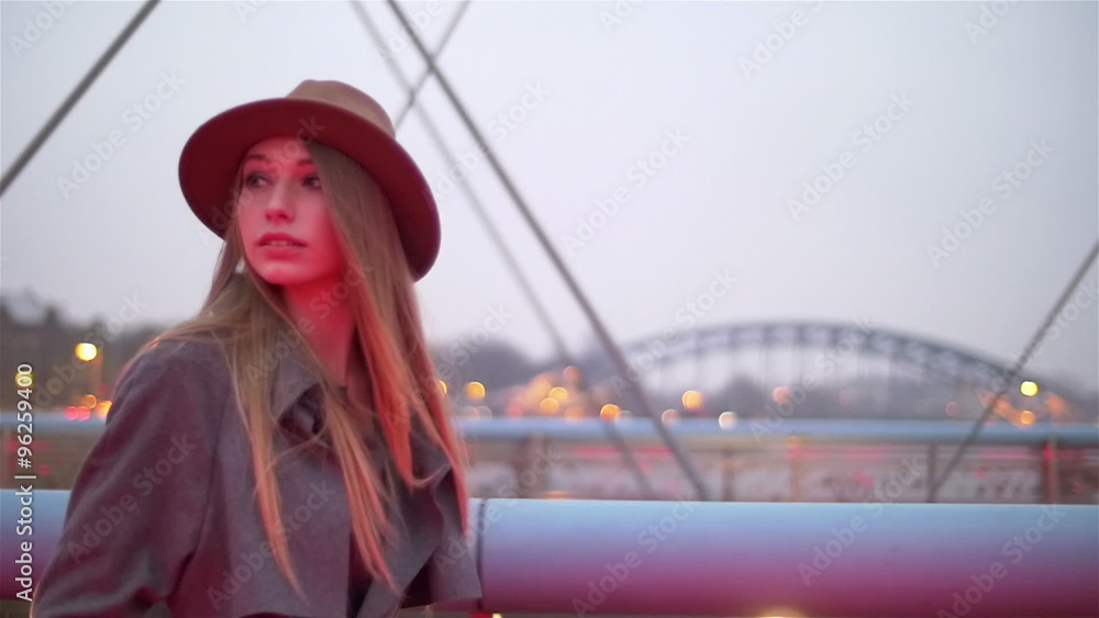 Fashionable top model walking a foot bridge in a trendy coat and hat ...