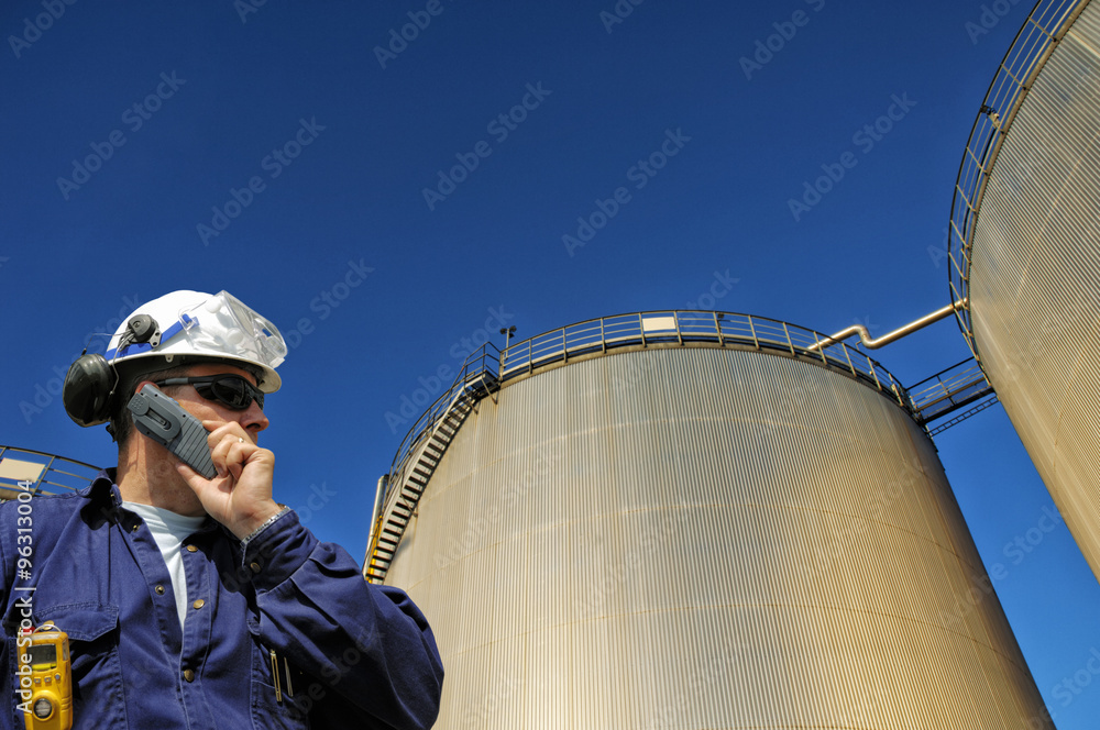 oil worker with large industrial fuel storage tanks inside refinery ...