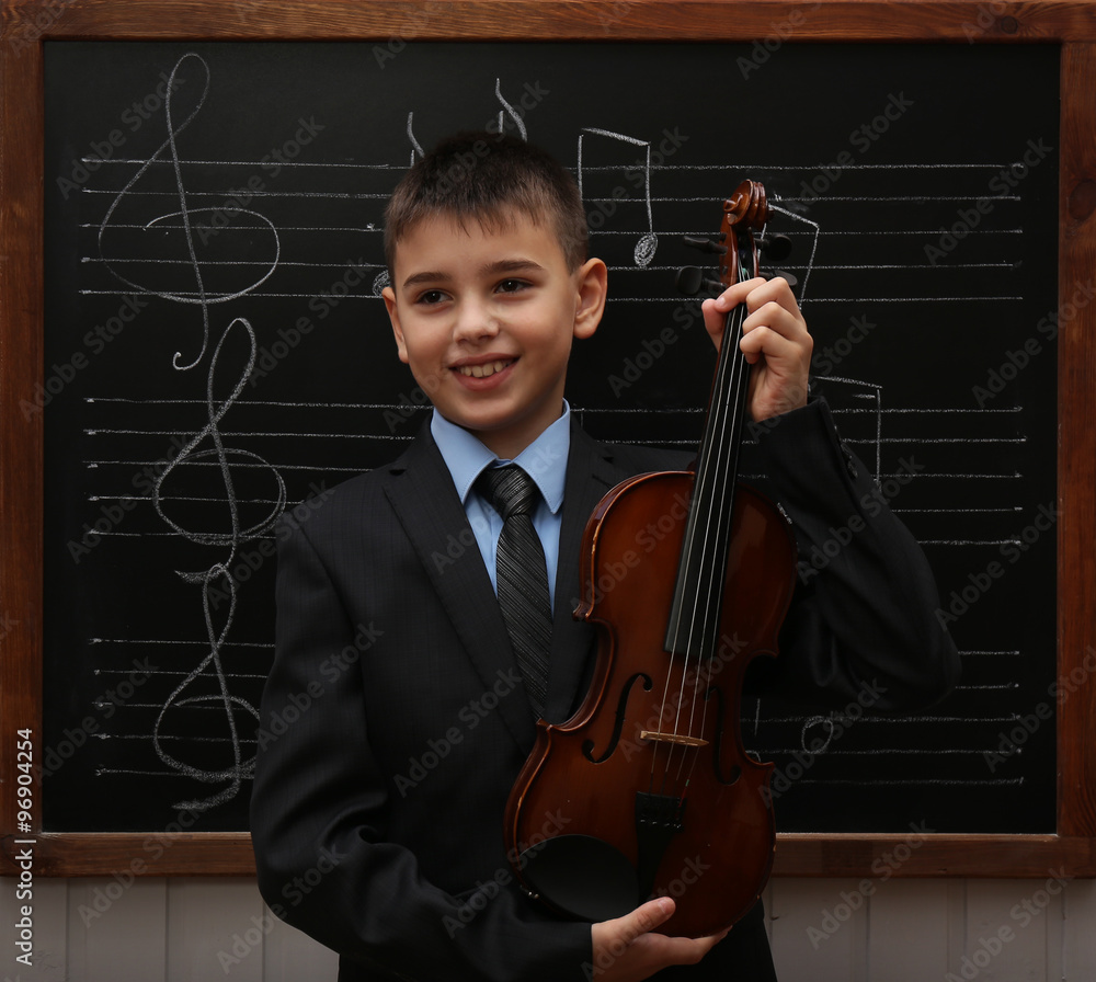 Young cute schoolboy holding the violin at the blackboard with musical ...