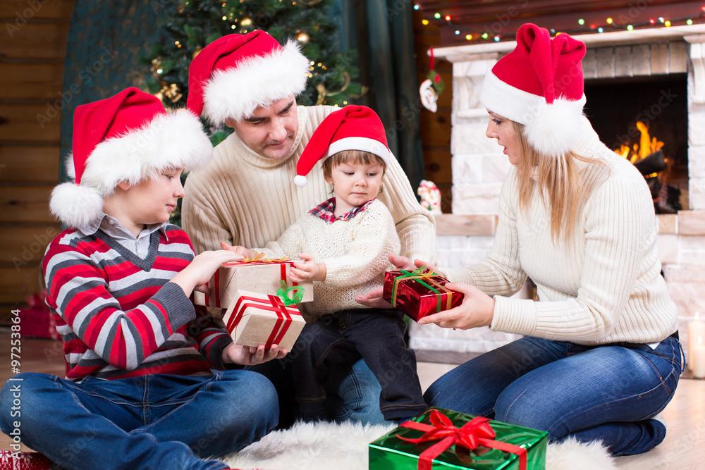 Happy family in red hats with gifts sitting at Christmas tree near ...