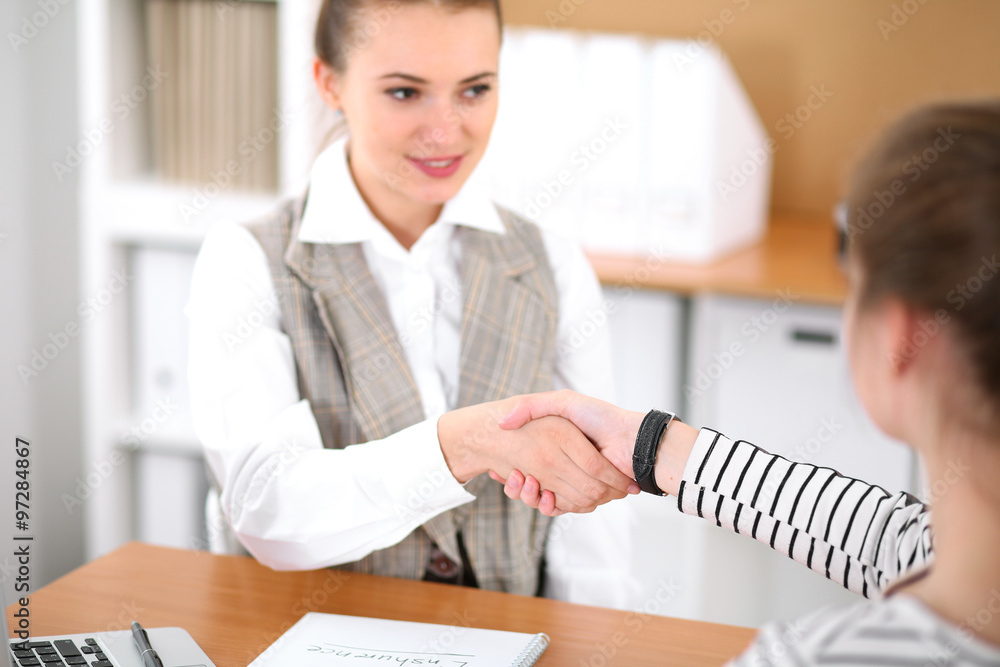 Young business woman shaking hands with a client at the office ...