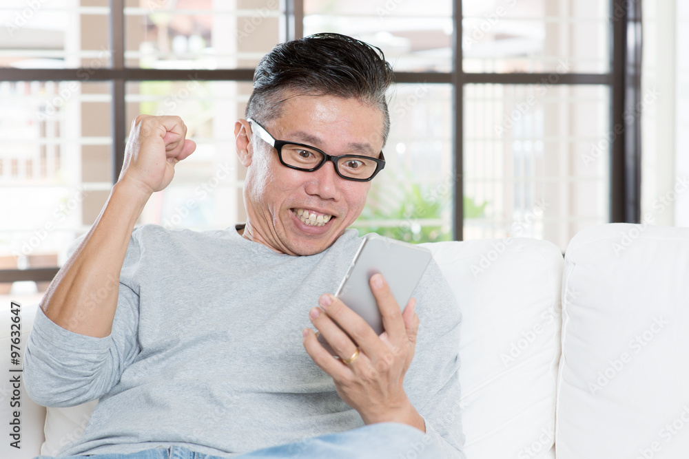 Mature Asian man celebrates success while using smartphone Stock Photo ...