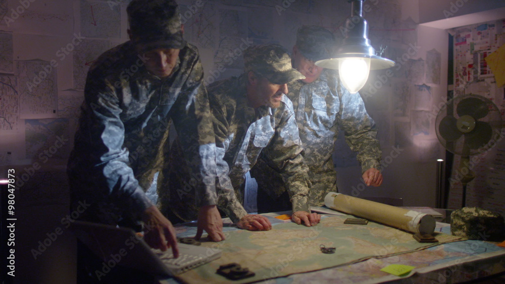 Military officers in army bunker, looking at map & discussing battle ...