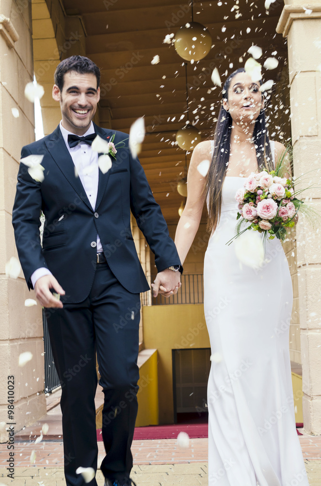 Bridal couple after the wedding under rain of rose petals and rice ...
